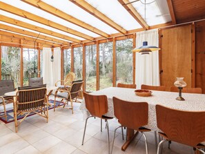 Espaço de refeições com uma mesa grande, cadeiras e vista para o exterior.