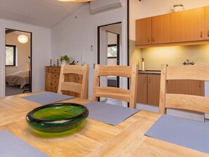 Quarto compacto com uma mesa de jantar, cadeiras, uma tigela de vidro verde, um armário de madeira e uma pequena planta.