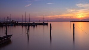 Um calmo areal marítimo ao pôr do sol, com barcos atracados e céu claro.