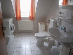 Uma casa de banho pequena e simples, com sanita, lavatório e máquina de lavar roupa.