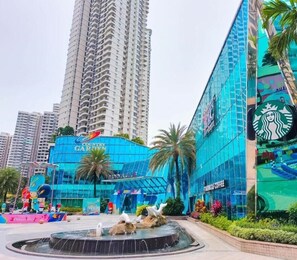 Um edifício moderno com o letreiro da Starbucks, uma fonte de água com patos e palmeiras.