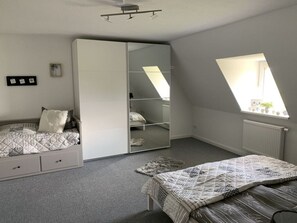 Quarto com cama, guarda-roupa, espelho, radiador e claraboia.