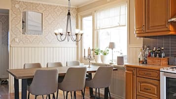 Cozinha com mesa de jantar, cadeiras, lustre, janela com cortinas e armários de madeira.