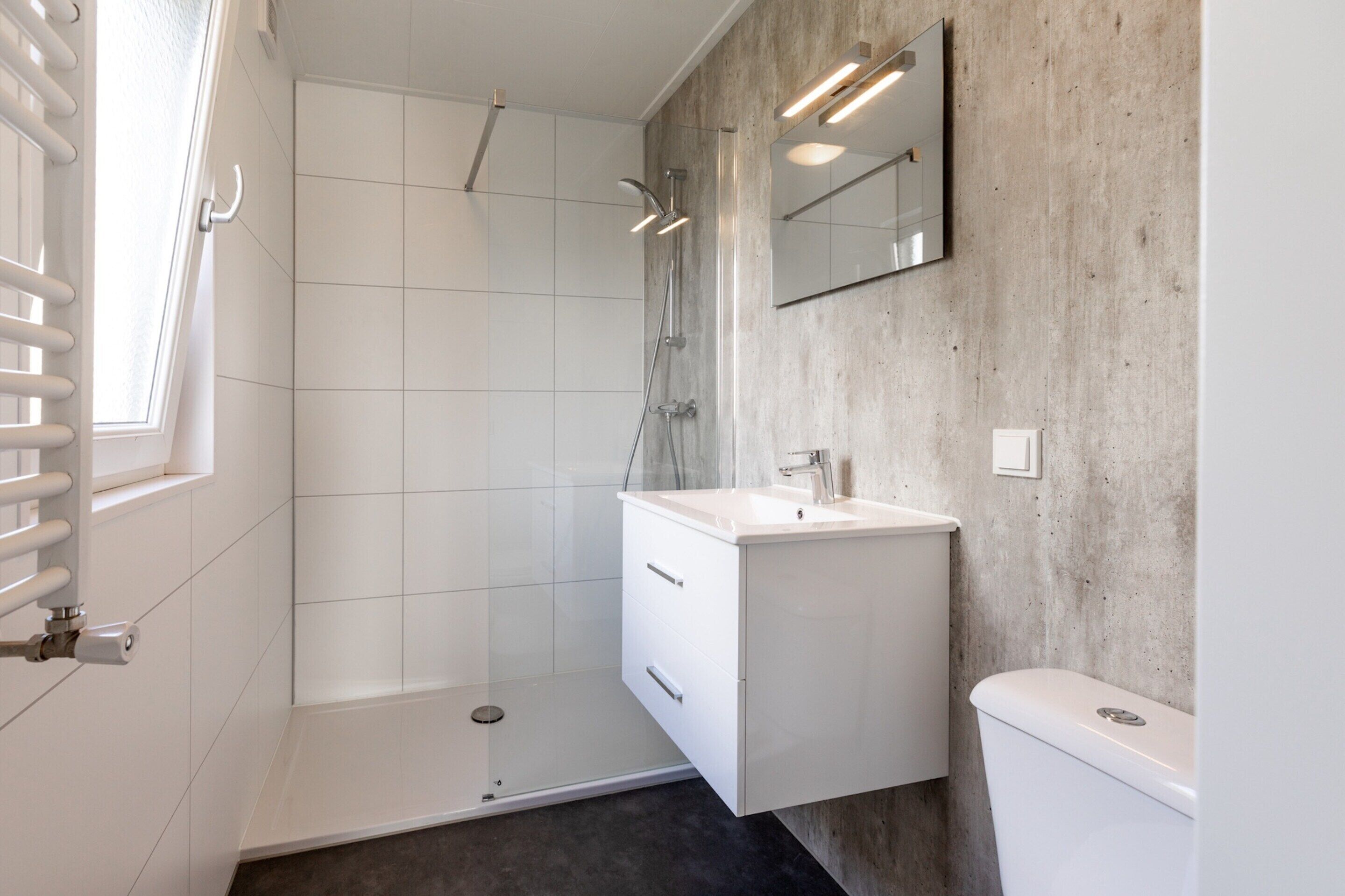 Uma casa de banho moderna com chuveiro em cabine de vidro, toucador branco com espelho e sanita.
