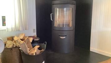 Um quarto com uma lareira a lenha preta, uma lixeira preta e uma pilha de lenha.