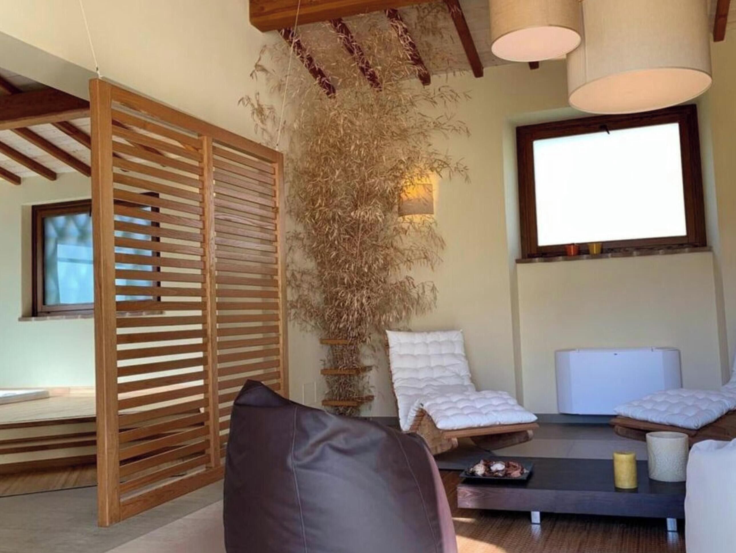 Quarto moderno com divisória de ripas de madeira, uma grande planta em vaso, sofá branco e cama com cabeceira branca.
