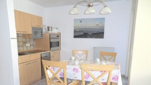 Cozinha compacta com armários de madeira, micro-ondas e área de jantar com mesa posta para quatro pessoas.