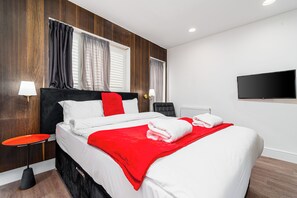Quarto de hotel moderno com uma cama grande, duas mesas de cabeceira, uma TV de tela plana e uma janela com cortinas.