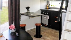 Cozinha moderna com bancada preta, dois banquetes, uma TV fixada acima da bancada e vista para o exterior.