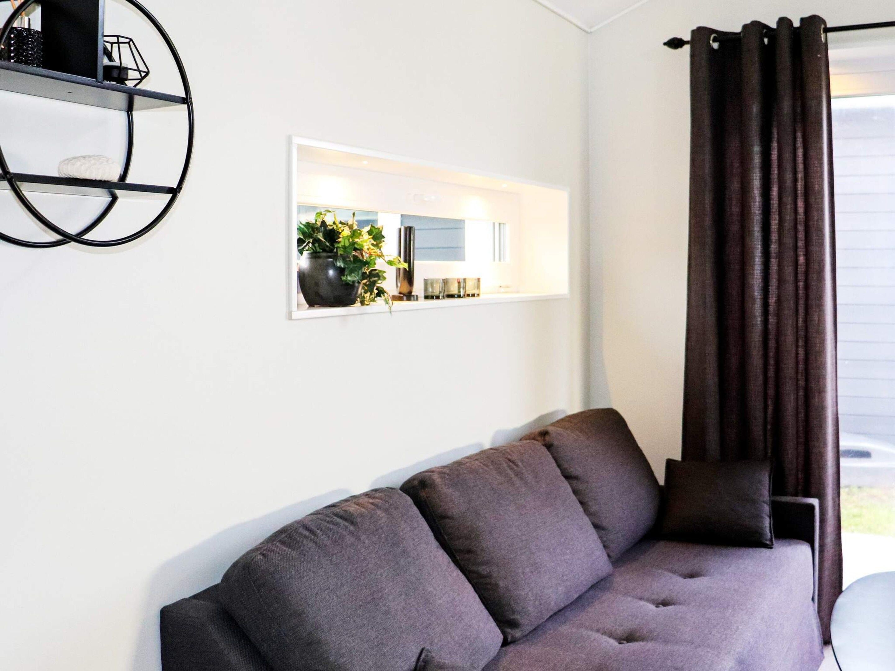 Uma sala de estar moderna com um sofá cinza escuro, uma estante de metal preto e um quadro com uma cozinha.
