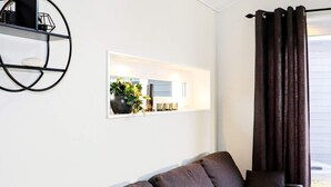 Uma sala de estar moderna com um sofá cinza escuro, uma estante de metal preto e um quadro com uma cozinha.