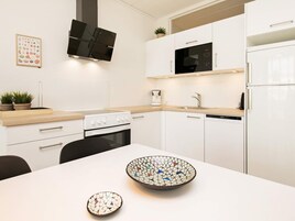 Cozinha moderna com armários brancos, fogão, micro-ondas e lava-louças. Duas tigelas decorativas estão sobre a mesa.