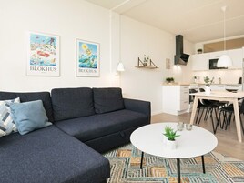Uma sala de estar moderna com um sofá escuro, uma mesa de centro redonda e duas obras de arte penduradas na parede intituladas 'BLOKHUS'.