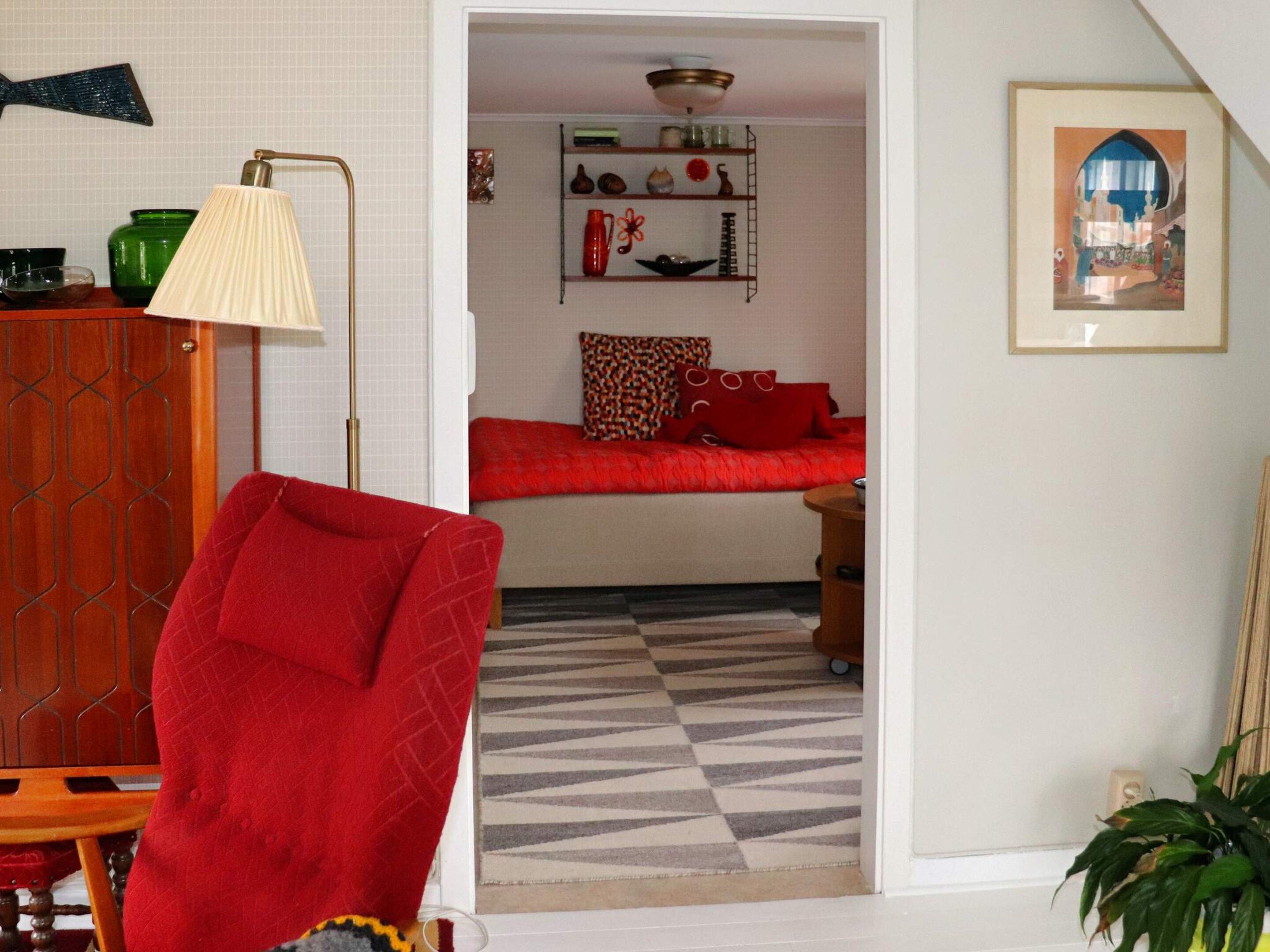 Quarto com sofá vermelho, luminária, tapete estampado e quadro na parede.