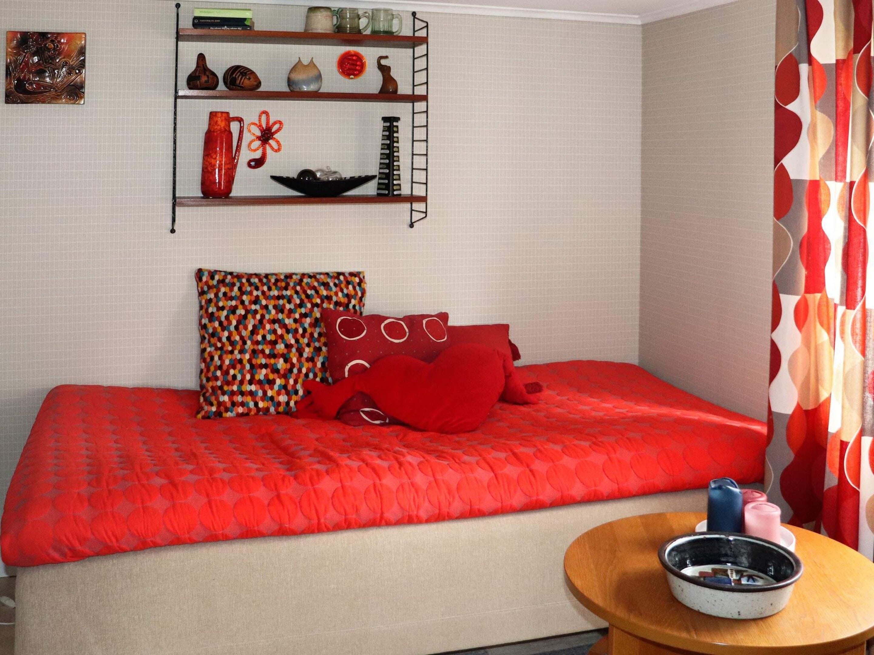Quarto com uma cama, uma mesa de madeira redonda e uma estante com objetos decorativos.