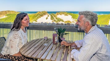 Um casal sentado à mesa de madeira, com vista para a praia e dunas.