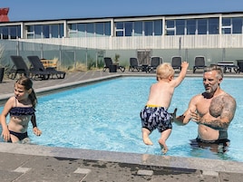 Piscina com cadeiras de praia e um edifício ao fundo.