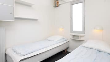 Quarto pequeno e limpo com duas camas de solteiro, uma janela e um prateleira na parede.