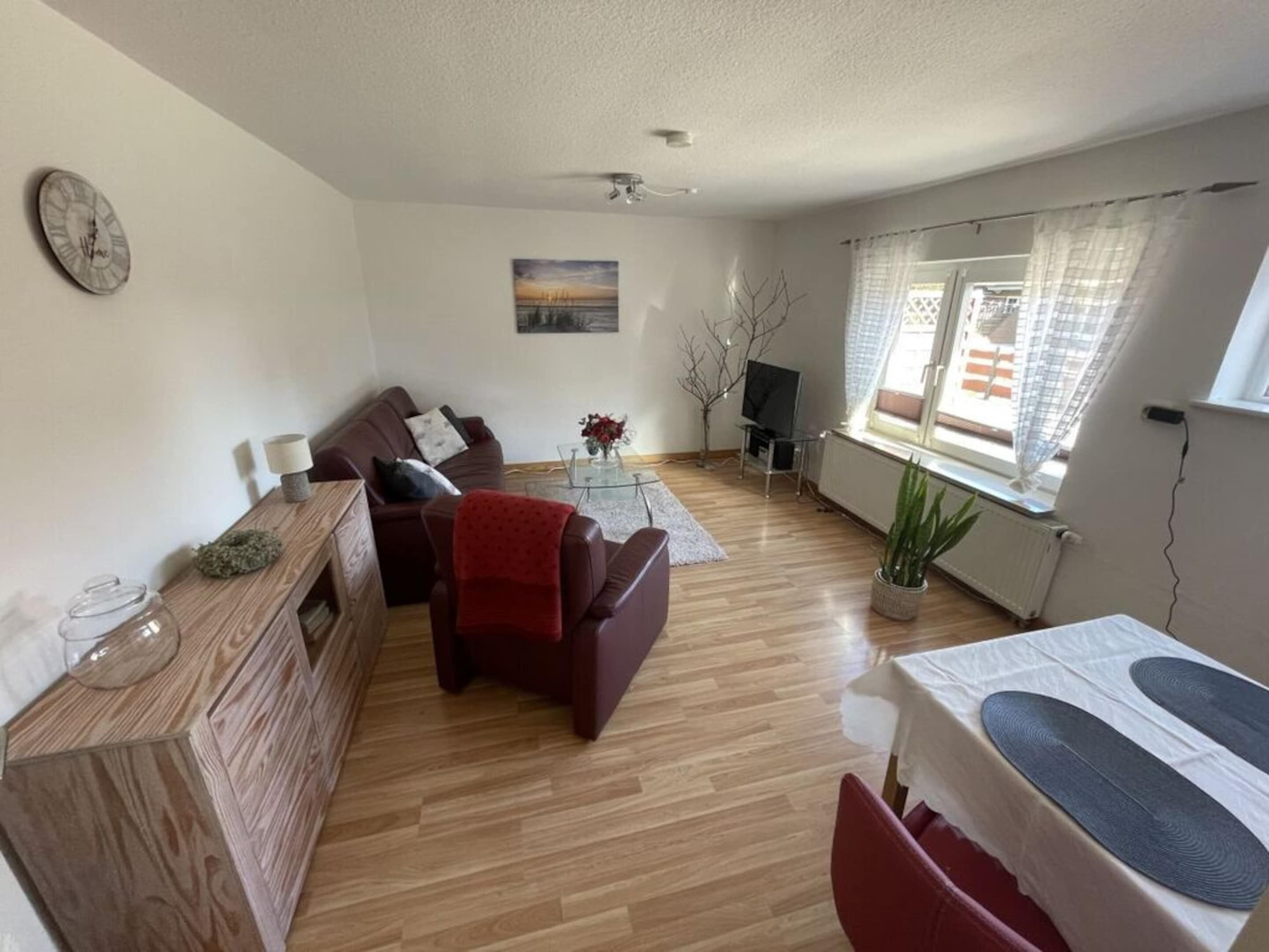 Sala de estar com sofá, mesa de centro e televisão. Há uma janela com cortinas e uma planta no chão.