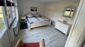 Quarto com cama, mesas de cabeceira, cômoda e janela.