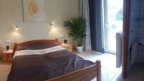 Quarto com cama de madeira, mesas de cabeceira com luminárias, um vaso de planta e vista através de uma porta de correr.