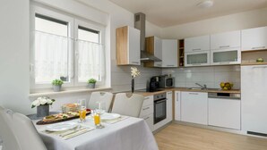Uma cozinha moderna com armários brancos, micro-ondas e fogão. Há uma mesa de jantar posta com pratos, copos e uma saladeira.