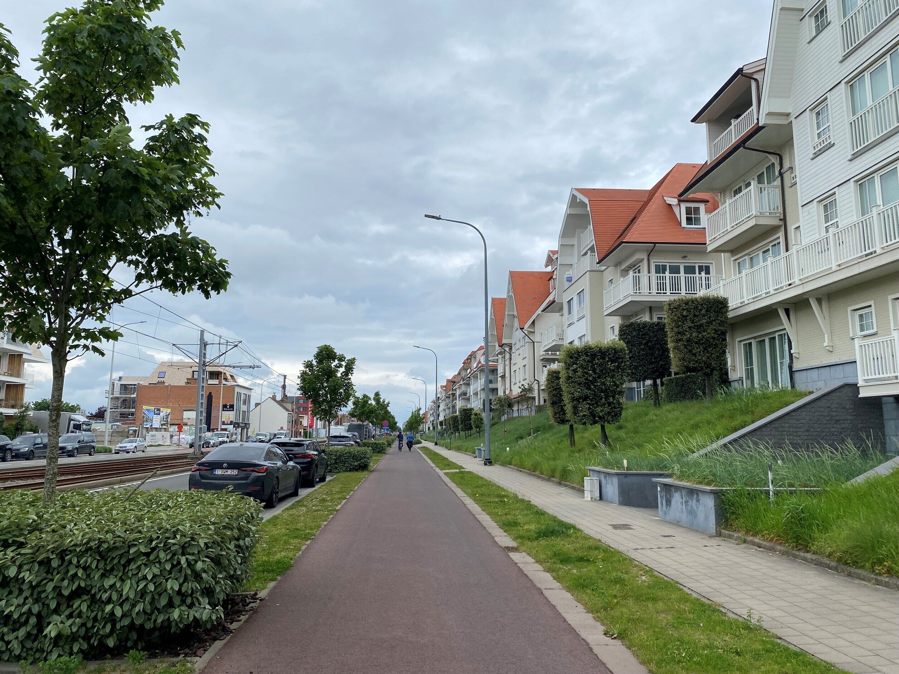 Rua residencial com calçada pavimentada, carros estacionados e edifícios de vários andares com varandas.