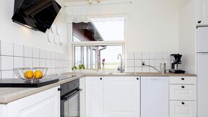 Cozinha moderna com armários brancos, forno embutido, máquina de lavar louça e janela com vista.
