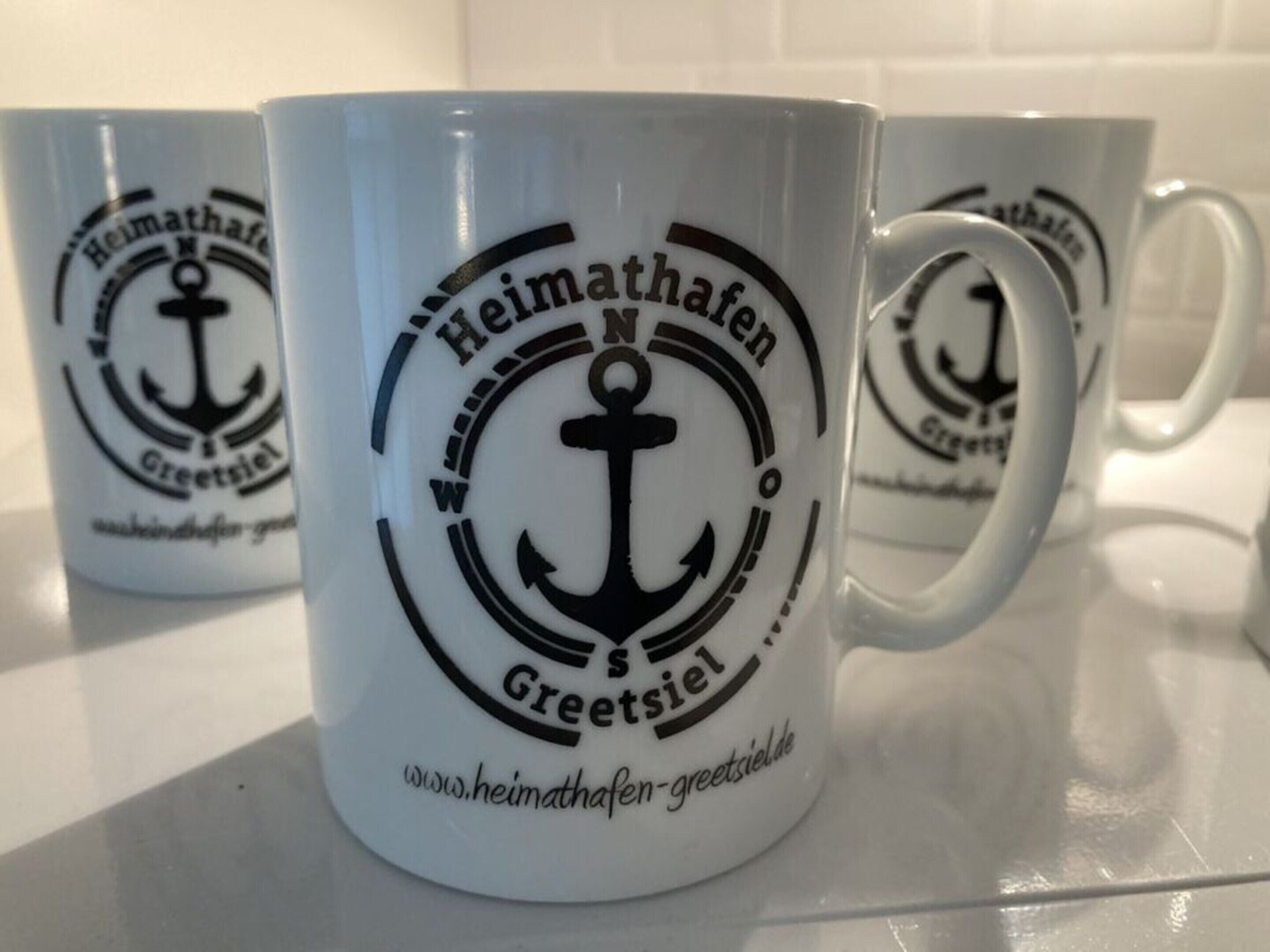 Uma caneca branca com um logotipo de ancora preta e texto.