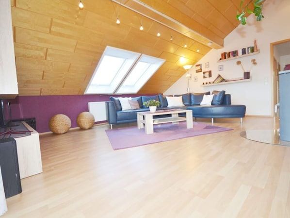 Uma sala de estar moderna no estilo loft, com teto inclinado, vigas de madeira e um amplo claraboia.