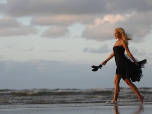 Uma pessoa caminhando na praia com ondas ao fundo.