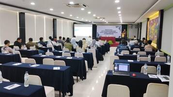 Sala de conferência com mesas, cadeiras e participantes.