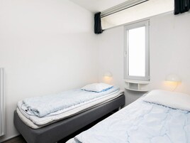 Quarto pequeno e limpo, com duas camas de solteiro, janela com cortinas e luzes de leitura fixadas na parede.