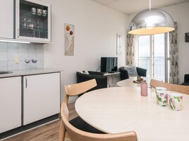 Cozinha moderna com área de refeições, TV e vista para o mar.