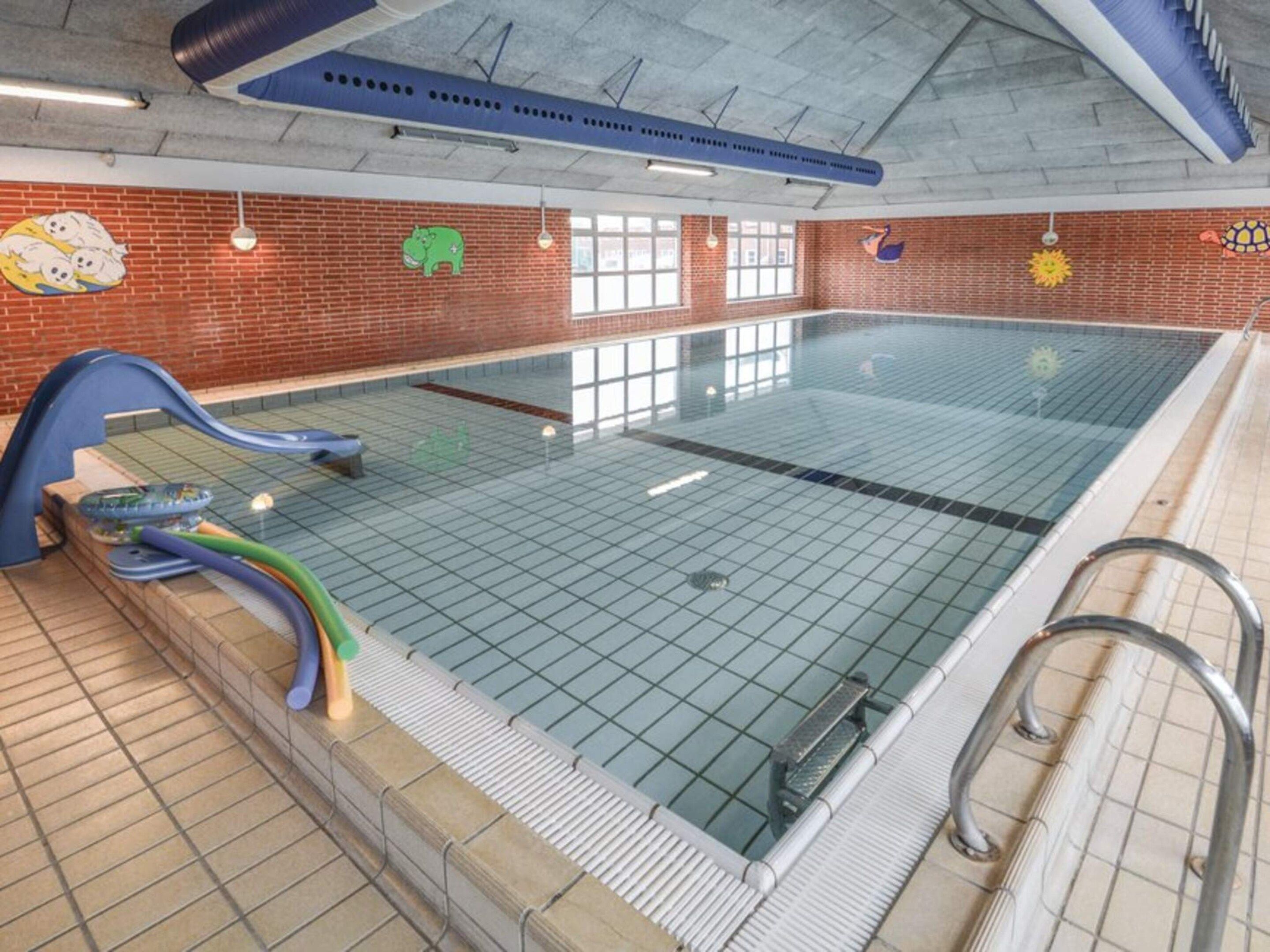Piscina interior com chão em mosaico, prancha de salto e escada.