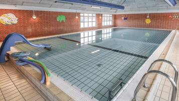 Piscina interior com chão em mosaico, prancha de salto e escada.
