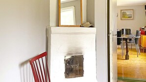 Quarto com parede branca, cadeira vermelha, espelho com moldura de madeira e área de refeições parcialmente visível, com cadeiras e mesa.