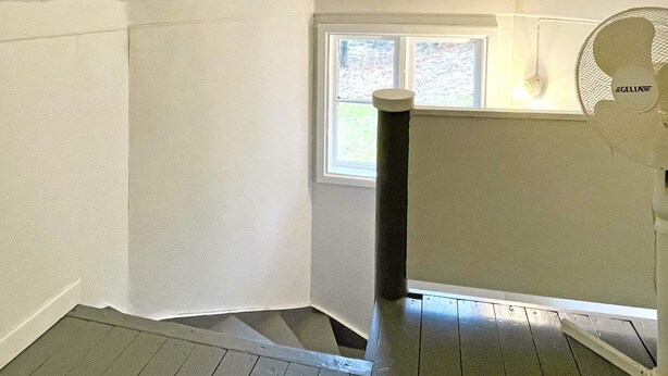 Quarto com teto inclinado, janela, radiador e ventilador.