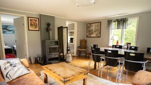 Uma sala de estar aconchegante com lareira, uma área de refeições com cadeiras e uma cozinha visível por uma porta aberta.