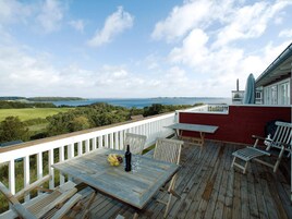 Um deck de madeira com mesa e cadeiras, com vista para a água e vegetação.