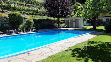 Uma piscina com borda de pedra, rodeada por um gramado e um pequeno edifício.