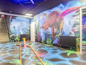 Espaço interior com um mural de uma cena pré-histórica, incluindo um grande dinossauro e plantas da era pré-histórica.