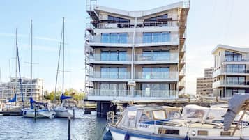 Um edifício de vários andares com varandas e grandes janelas, localizado à beira de um porto com barcos atracados.