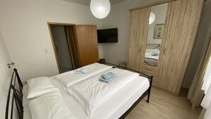 Quarto com cama, guarda-roupa de madeira e televisão na parede.