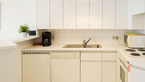 Uma cozinha moderna com armários brancos, máquina de lavar louça, pia, cafeteira e torradeira.