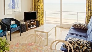 Sala de estar com televisão, sofá, mesa e vista para a praia.