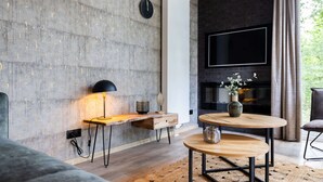 Uma sala de estar moderna com parede de concreto, lareira, televisão de tela plana e mesa de madeira redonda.