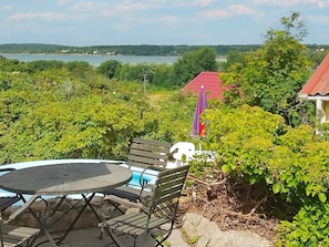 Um pátio com uma mesa redonda e cadeiras, uma piscina pequena e vista para um lago e colinas.