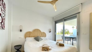 Quarto com cama, mesas de cabeceira, ventoinha no teto e vista para o exterior.