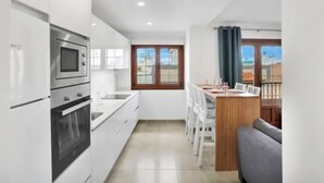 Uma cozinha moderna com armários brancos, forno embutido e área de jantar com mesa e cadeiras.